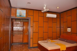 Quarto de hotel com um guarda-roupa de madeira, uma cama com manta amarela e um aparelho de ar condicionado na parede.