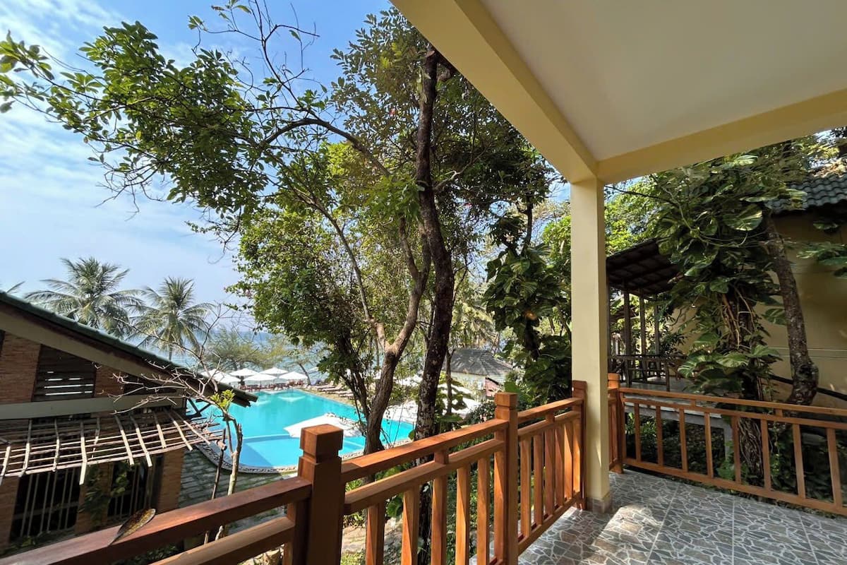 Varanda de madeira com vista para uma piscina e palmeiras.