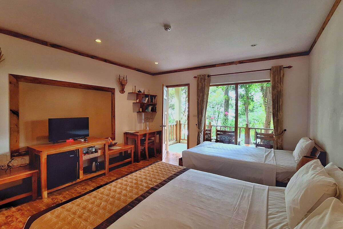 Quarto de hotel com duas camas, televisão, escrivaninha e estante de livros.
