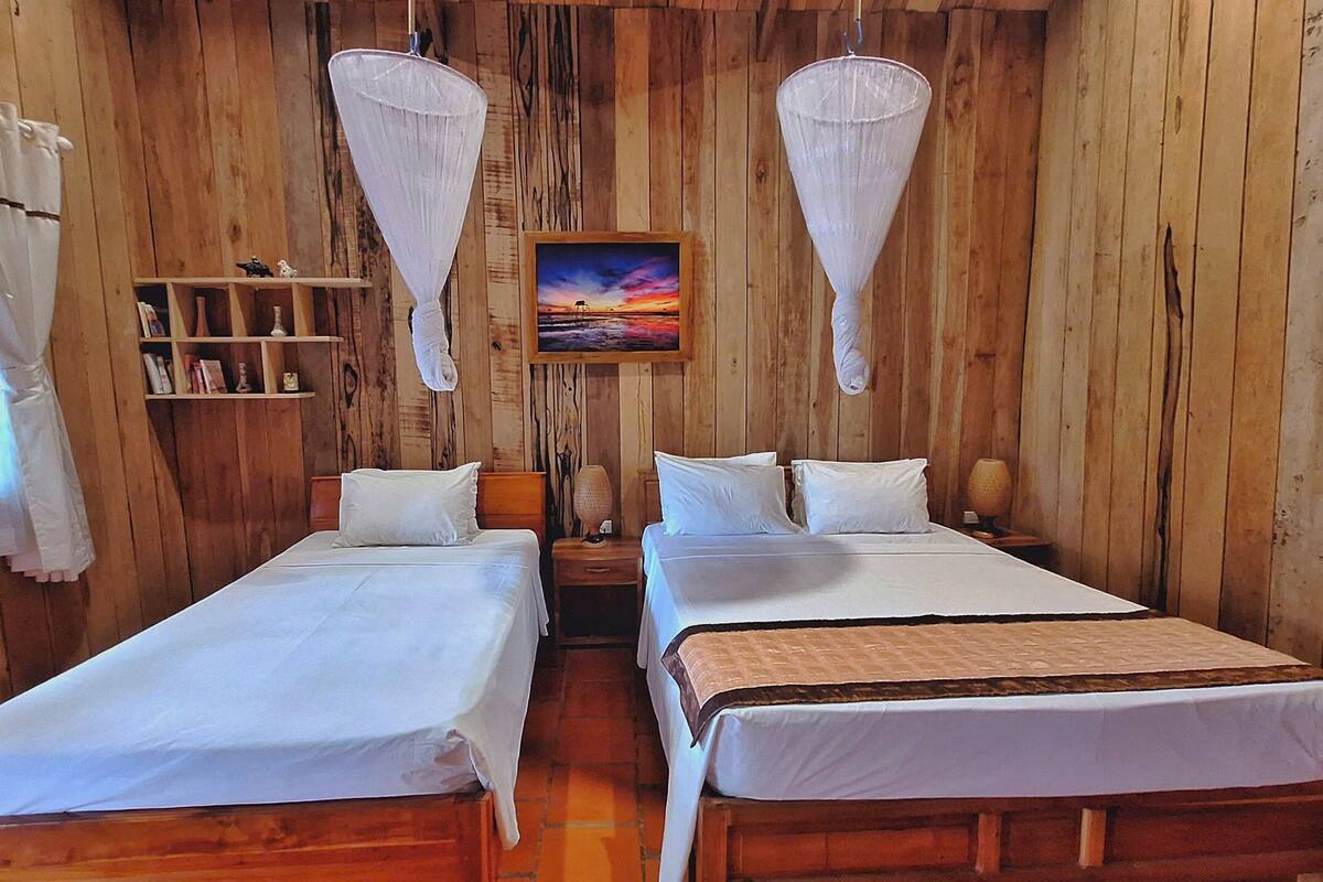Quarto com duas camas de solteiro, paredes de madeira, uma estante com objetos decorativos e um quadro sobre as camas.