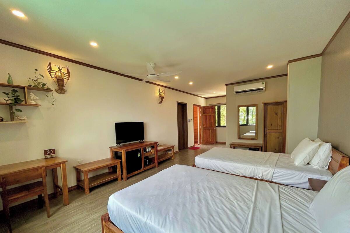 Quarto de hotel com duas camas, televisão, mobiliário de madeira e ventoinha no teto.