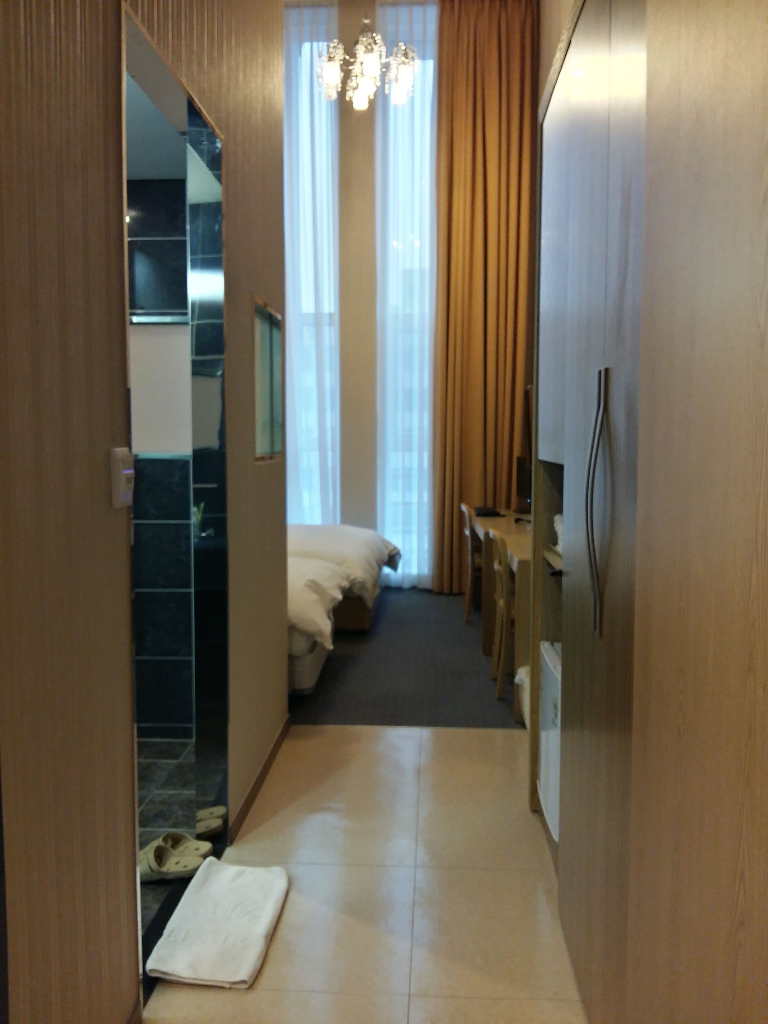 Um corredor estreito com uma cama, uma escrivaninha e um frigorífico.