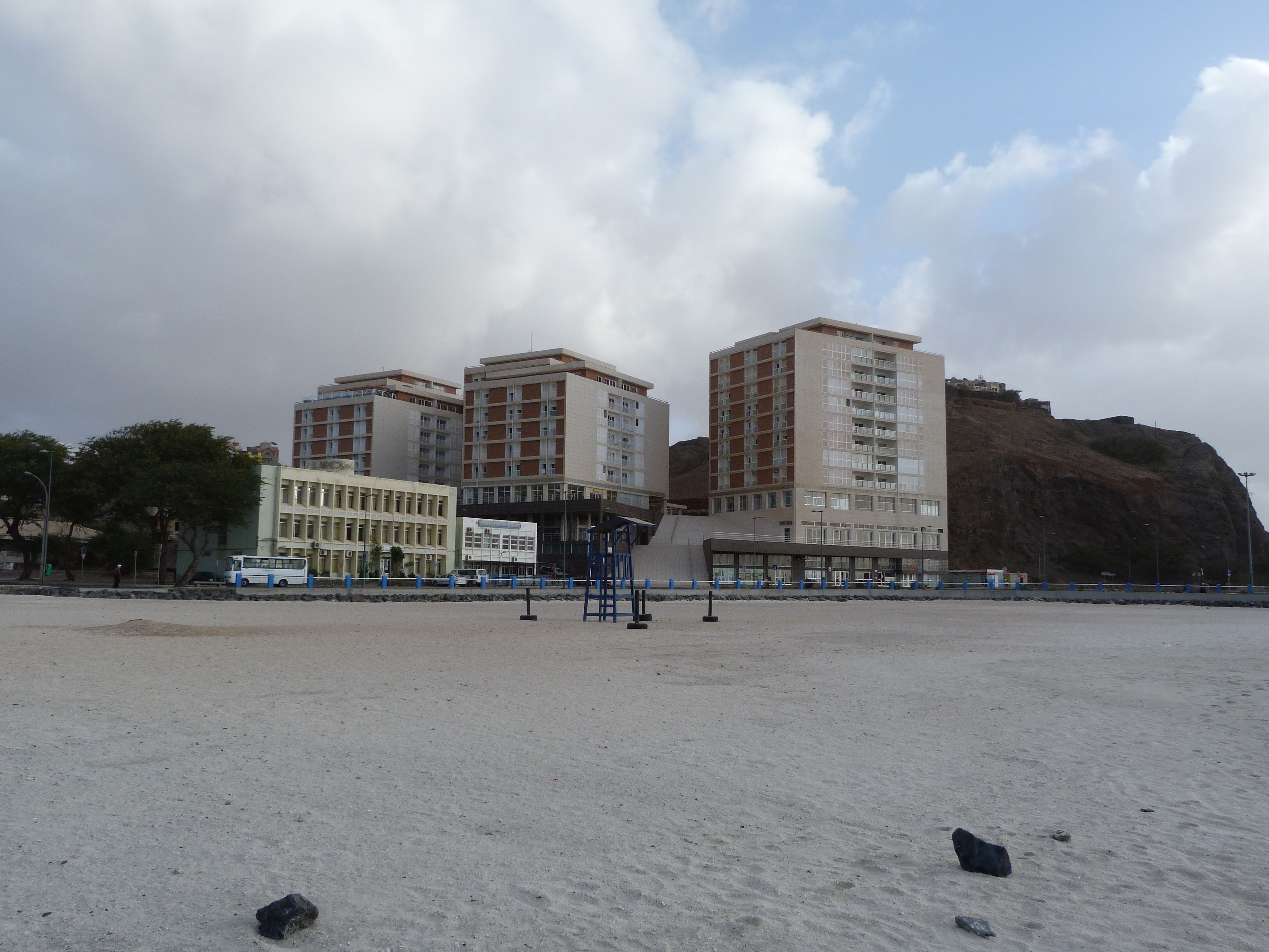 Uma praia arenosa com um conjunto de edifícios altos ao fundo.