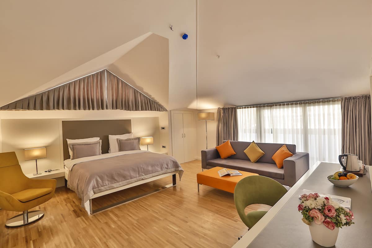 Quarto de hotel moderno com cama beliche, sofá, mesa de jantar e uma cadeira verde.