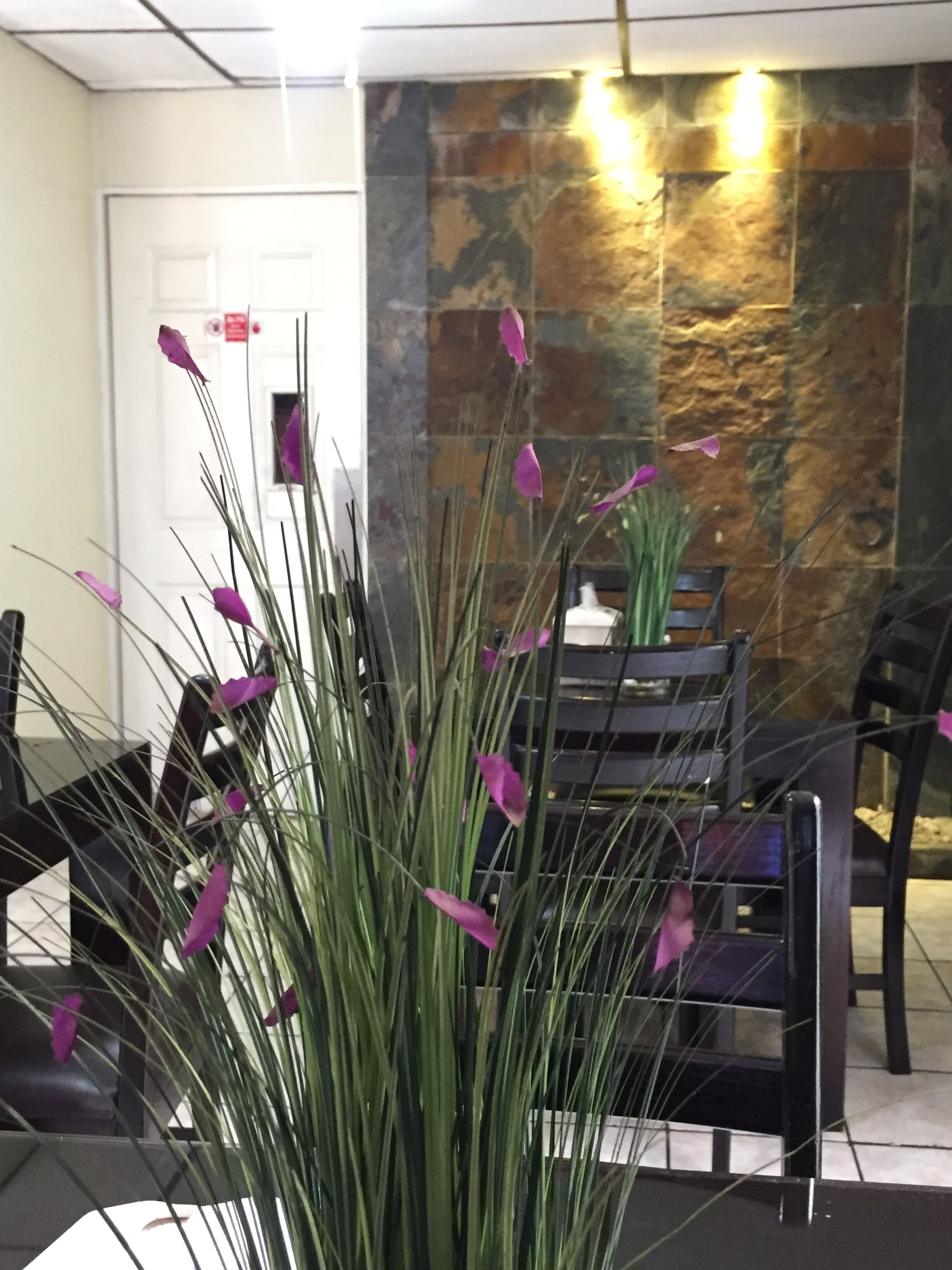 Uma área de recepção com balcão, cadeiras e uma planta ornamental com flores roxas.