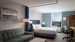 Quarto de hotel com cama, sofá, escrivaninha e vista para montanhas.