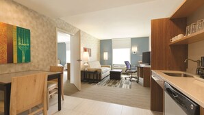 Uma cozinha moderna com lava-louças, uma sala de jantar com mesa e cadeiras, e uma sala de estar com sofá e luminária.
