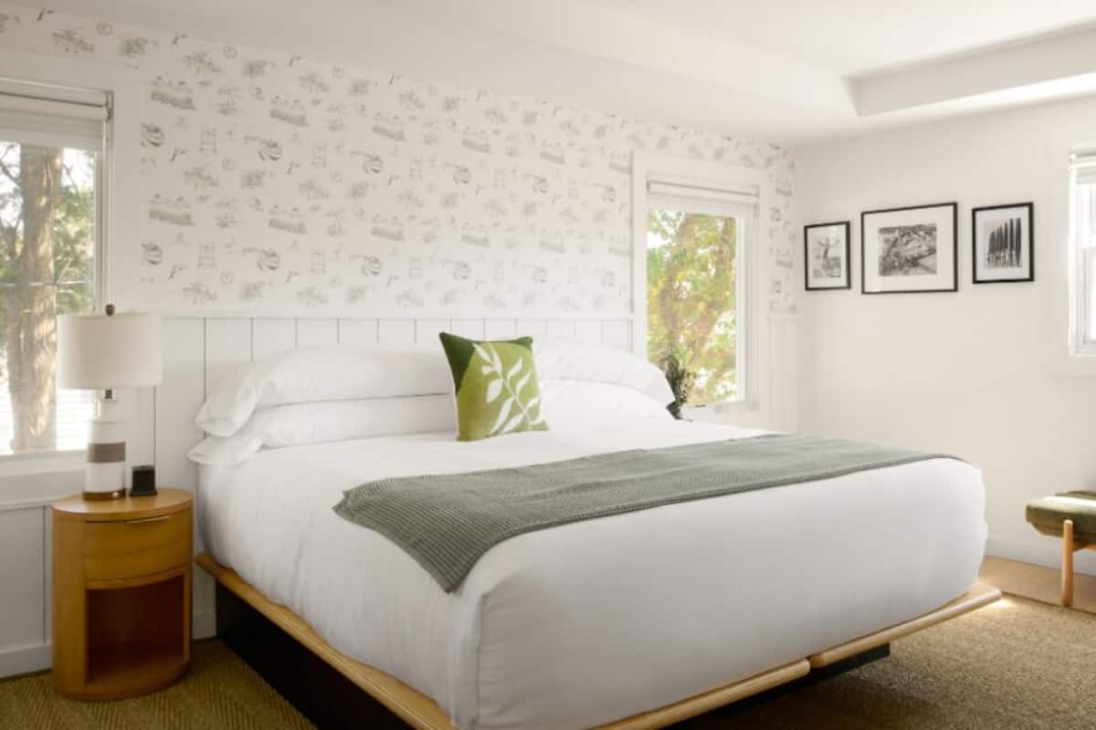 Quarto com cama, mesa de cabeceira, abajur, janela e parede com quadros.