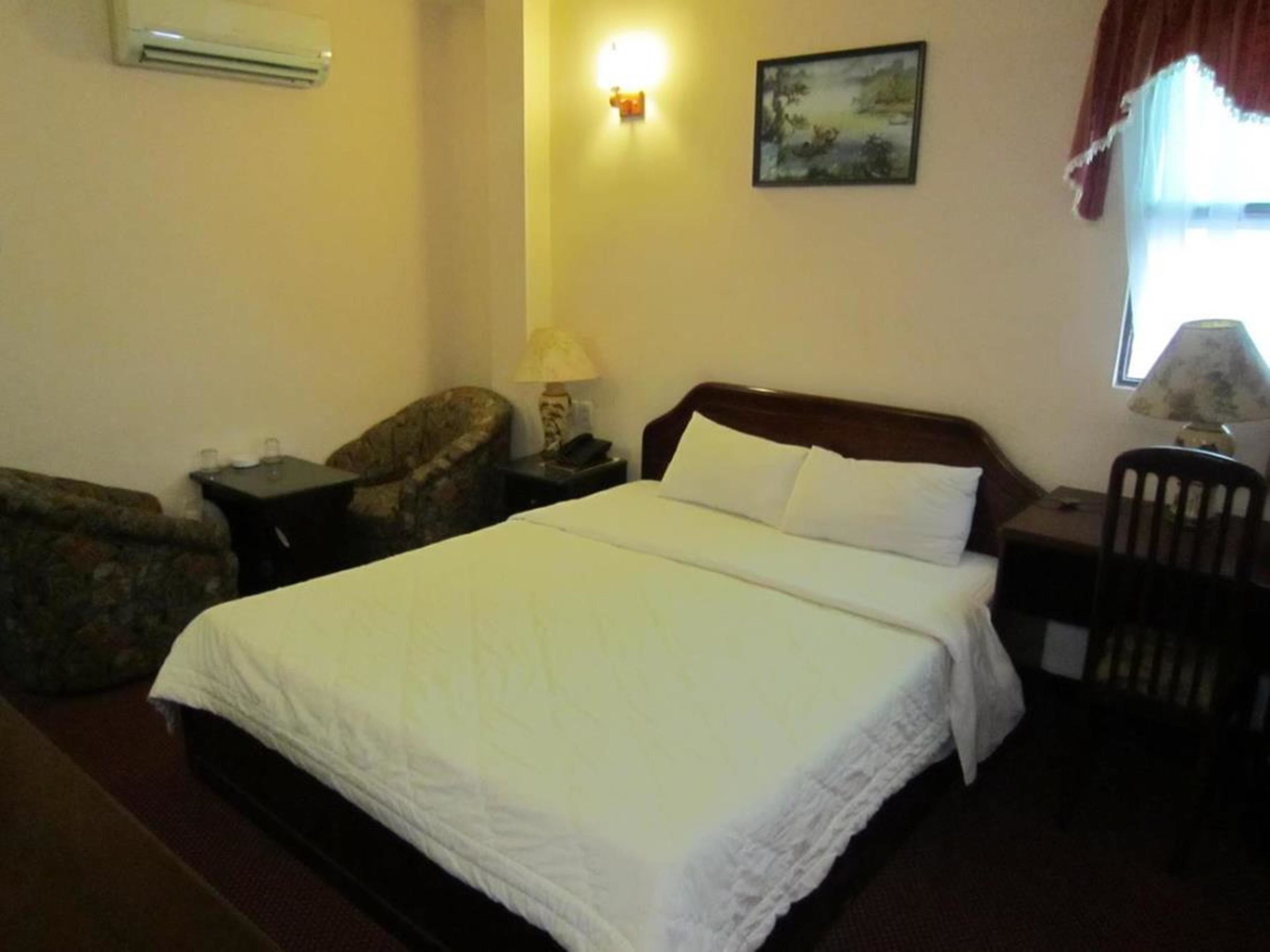 Quarto de hotel com cama, poltrona, escrivaninha e luminária.