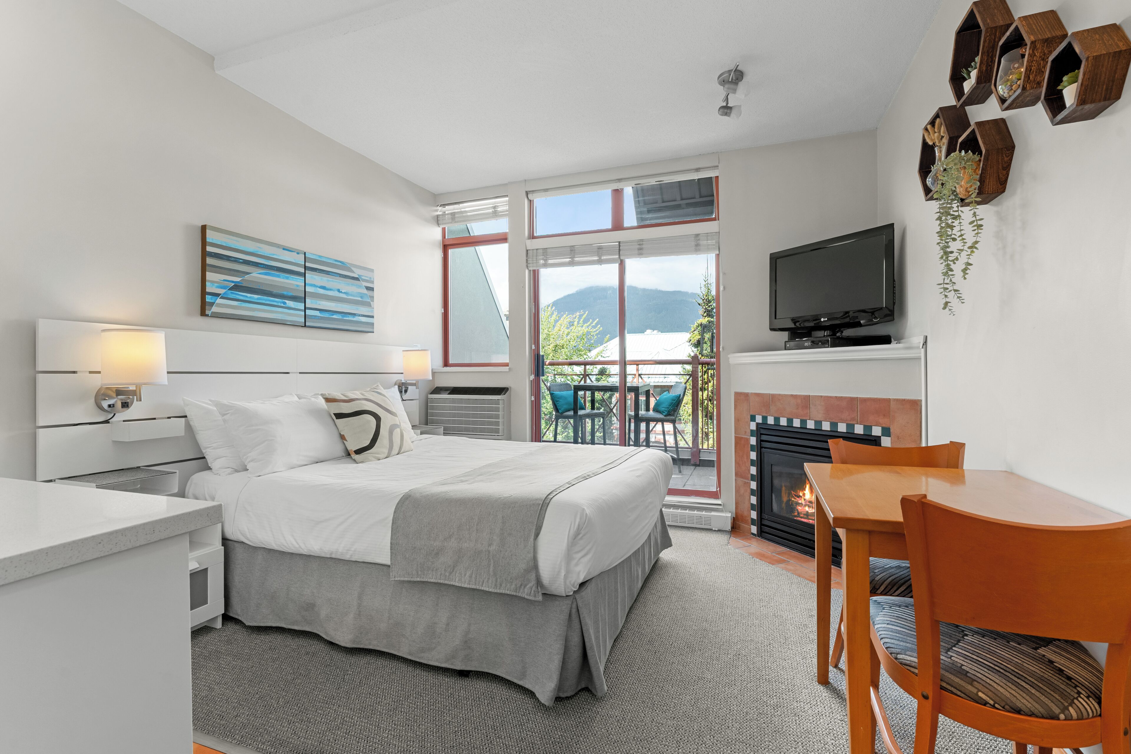 Quarto de hotel moderno com cama, mesa de cabeceira, luminária, televisão e lareira.