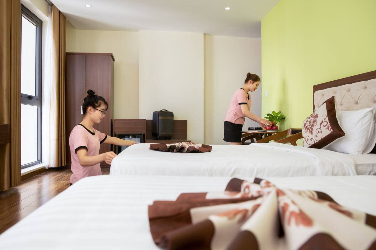 Quarto de hotel com duas camas, uma escrivaninha, uma cadeira, uma televisão e uma janela com cortinas.