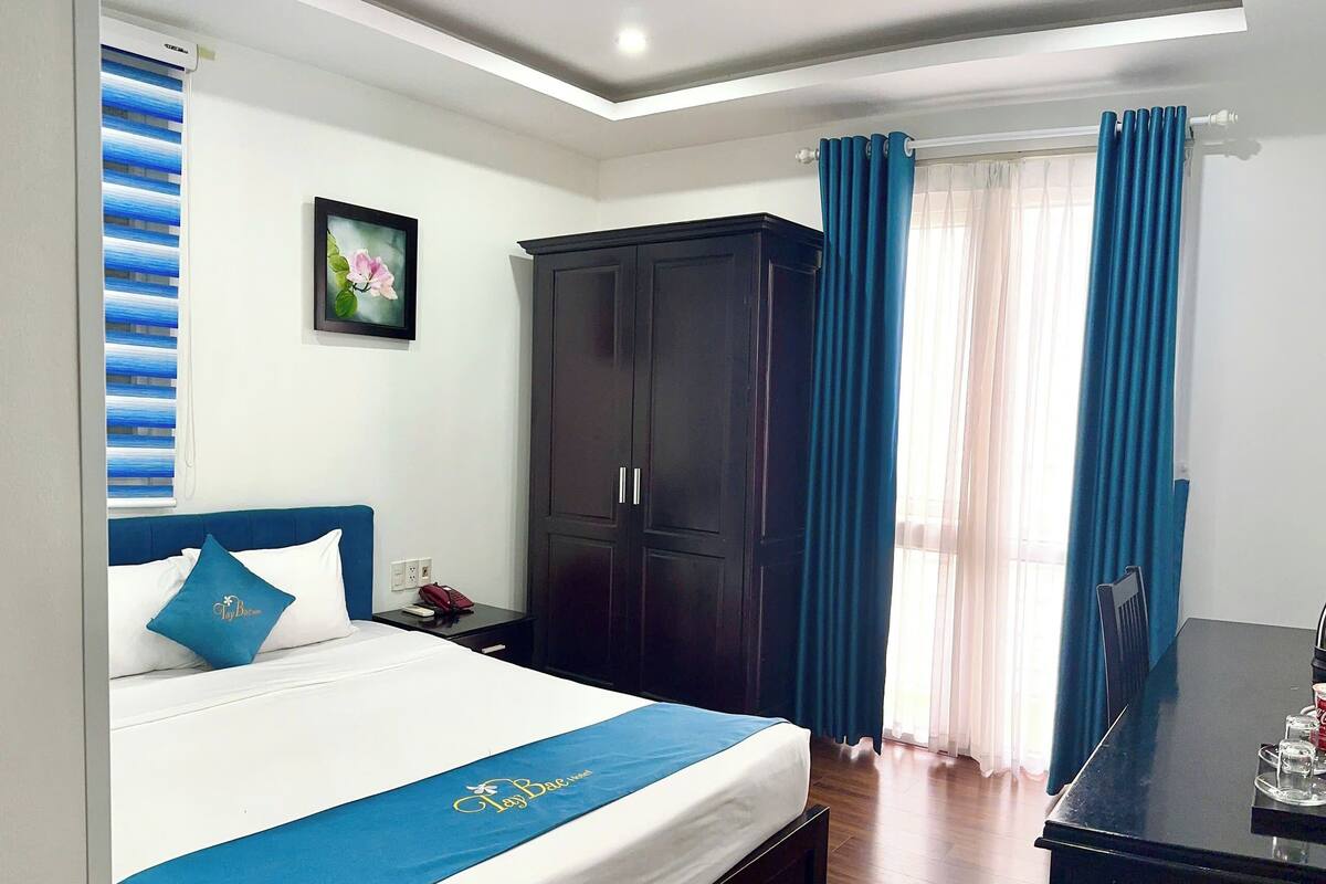 Quarto com cama, guarda-roupa, escrivaninha e janela com cortinas.