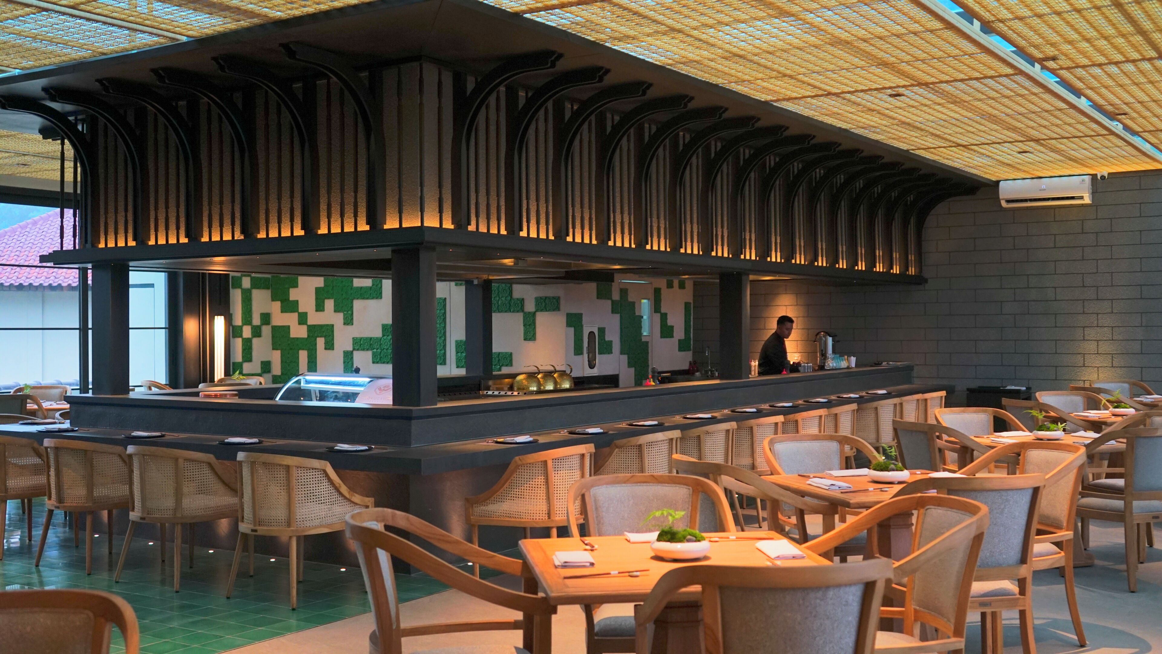 Um restaurante com design moderno, destacando uma área de bar central, diversas opções de assento e uma estrutura de teto singular.