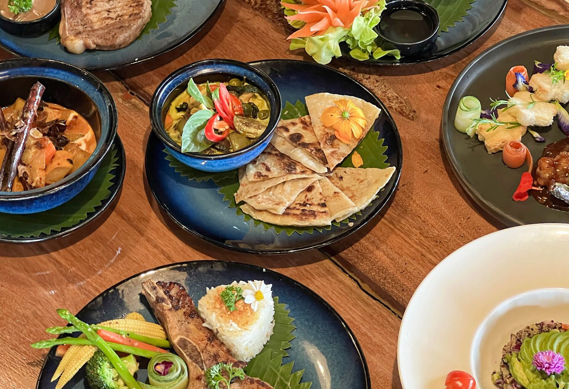 Diversos pratos sobre uma mesa de madeira, incluindo uma tigela de sopa, carne grelhada e pães achatados.
