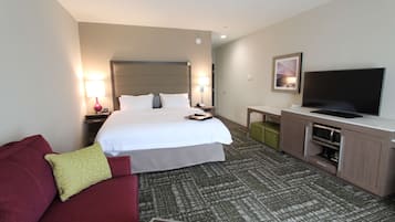 Quarto de hotel com cama, televisão, escrivaninha, sofá e piso coberto por carpete.