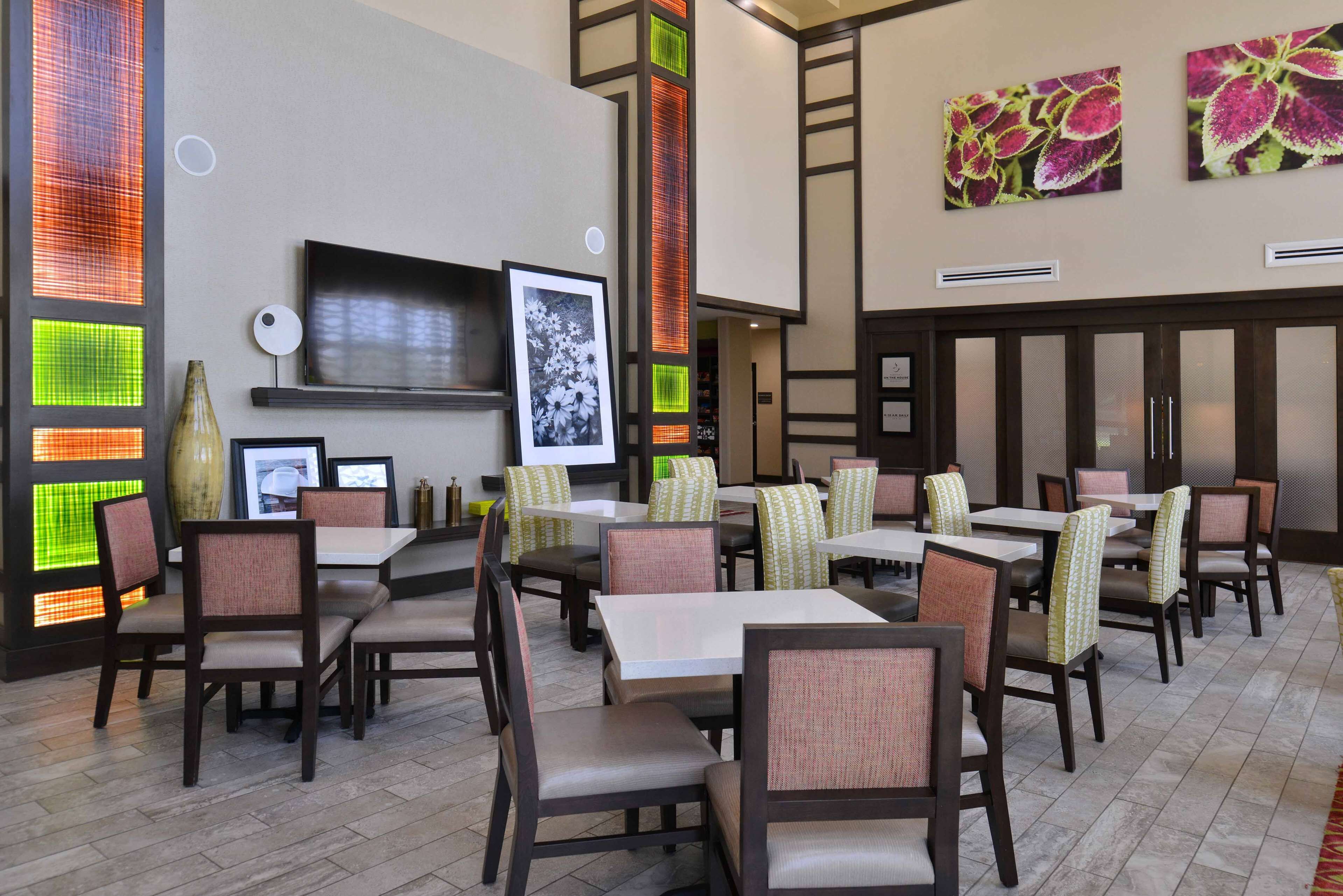 Um restaurante com várias mesas e cadeiras, uma televisão e painéis decorativos na parede.