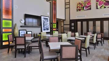 Um restaurante com várias mesas e cadeiras, uma televisão e painéis decorativos na parede.