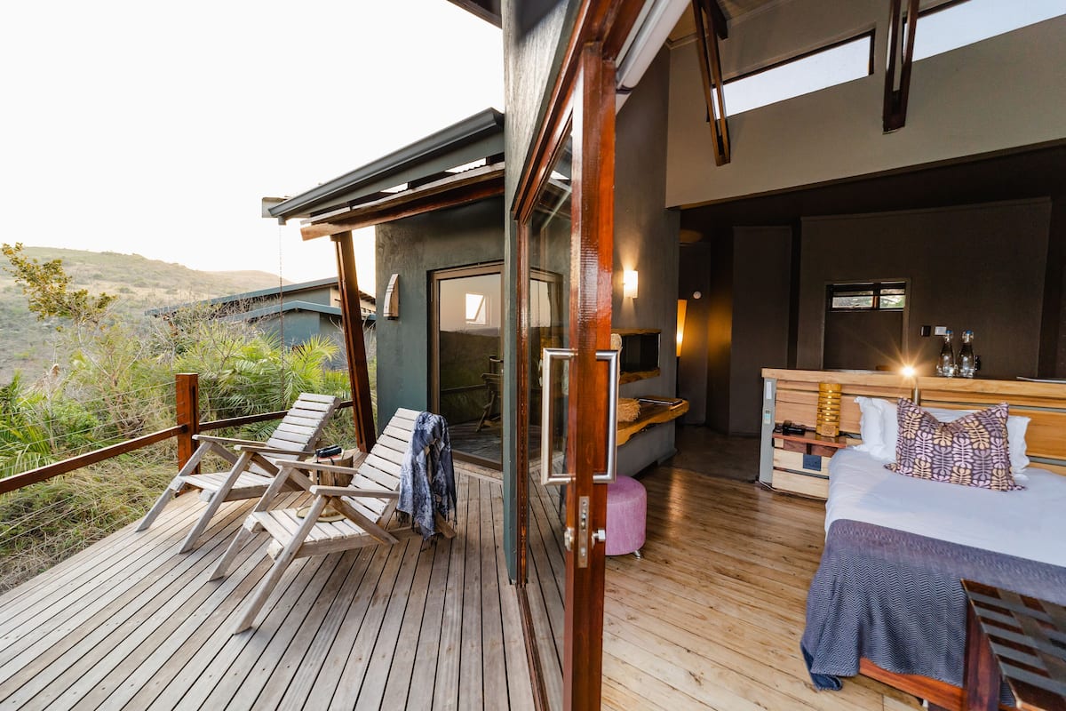 Um deck de madeira com espreguiçadeiras, cama com vista e uma pequena cozinha.