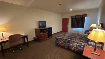 Quarto de hotel com cama, escrivaninha, cadeira, televisão, cômoda e duas luminárias.