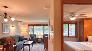 Quarto aconchegante com cama, sofá, mesa de jantar e cadeiras. Janelas oferecem vista para o exterior.