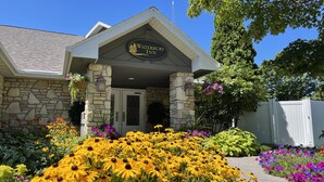 Entrada de hotel com fachada de pedra, uma placa com o texto 'Waterbury Inn' e uma variedade de flores coloridas na frente.