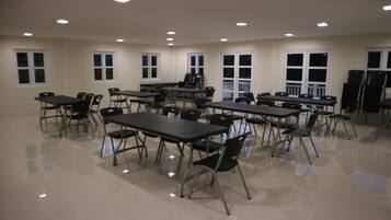 Uma sala de aula com mesas e cadeiras dispostas em fileiras, amplas janelas e luminárias no teto.