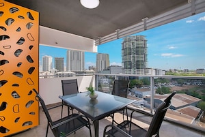Uma varanda com mesa e cadeiras de vidro, um vaso de planta e vista para o horizonte da cidade.
