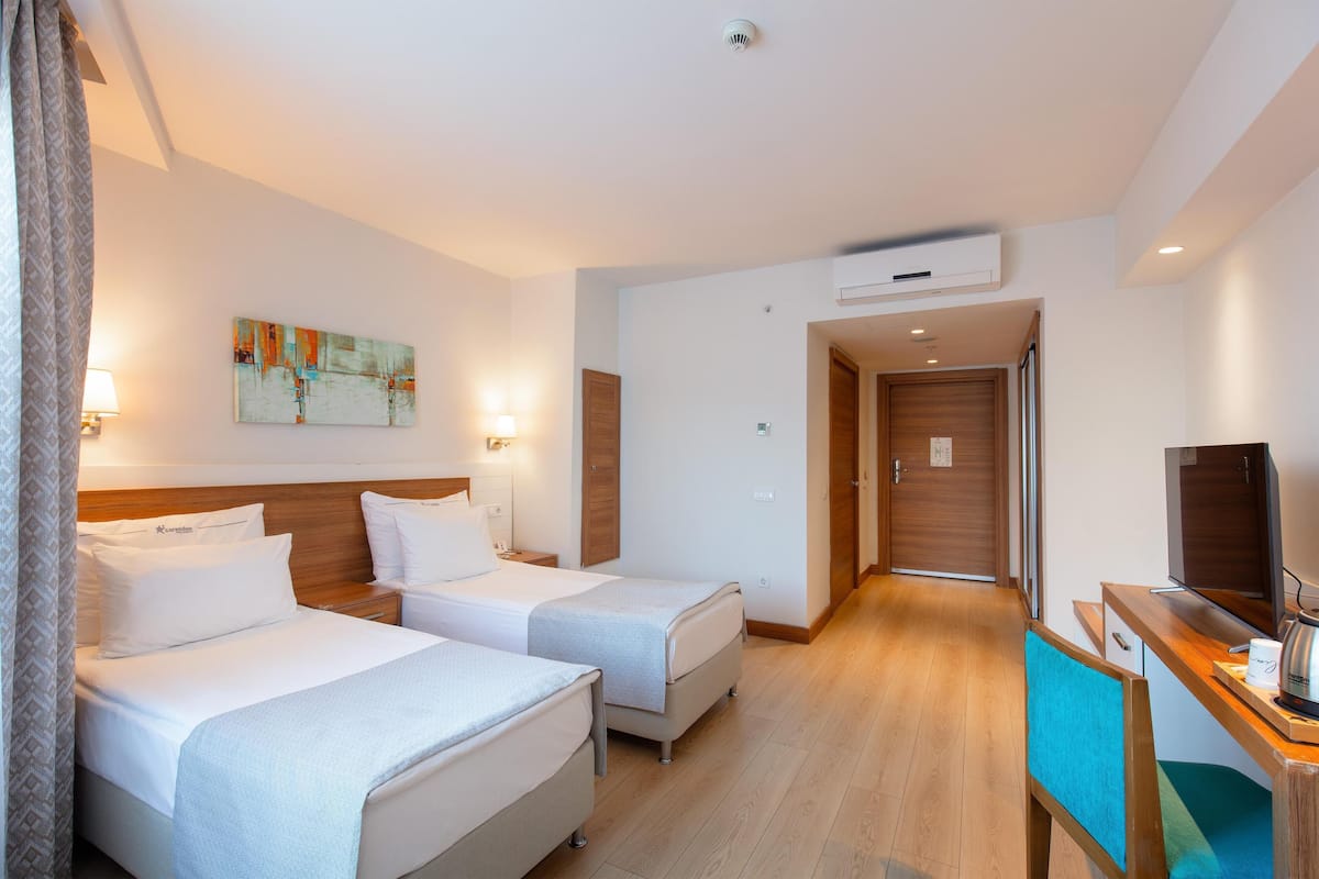 Quarto de hotel com duas camas, uma escrivaninha com cadeira, televisão e um quadro na parede.