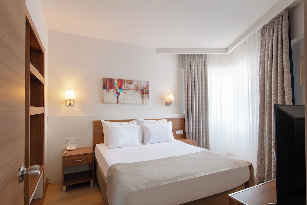 Quarto de hotel com cama, mesas de cabeceira, televisão e um quadro na parede.