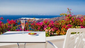 Mesa com uma taça de champanhe e um prato de frutas, com vista panorâmica para montanhas e o mar.