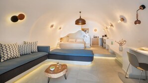 Um interior moderno e minimalista com teto curvo, área de estar central com sofá e mesa de centro, cama com cabeceira original e uma pequena cozinha compacta ao fundo.