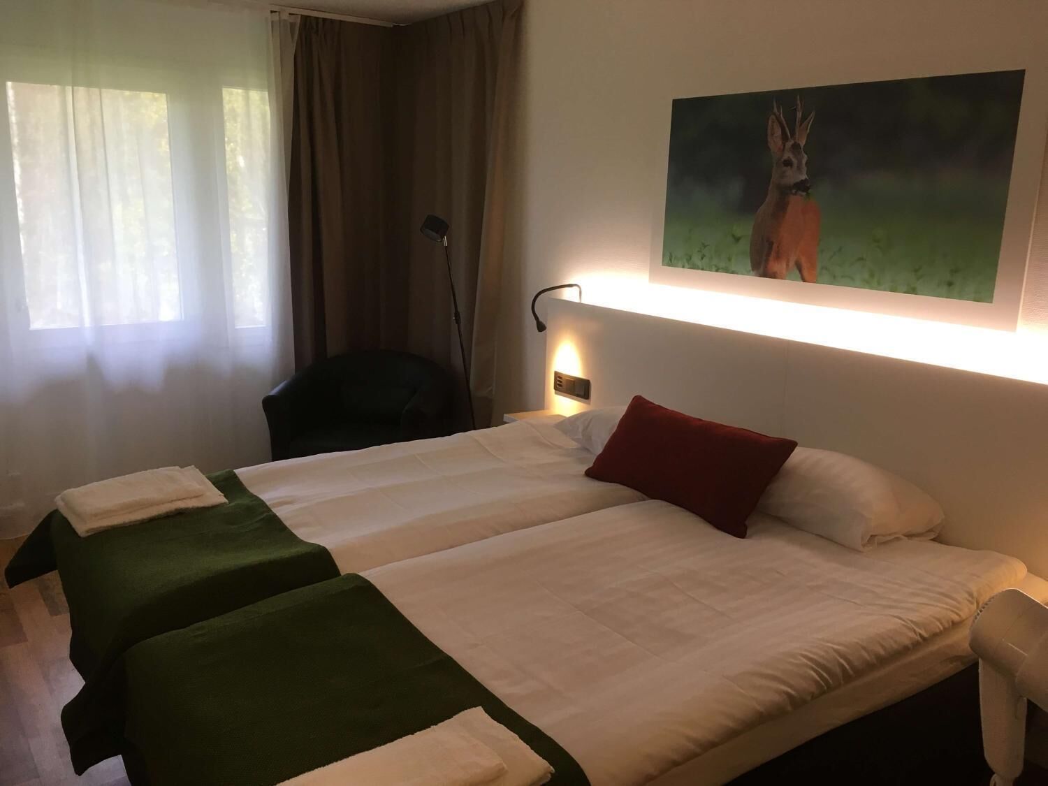 Quarto de hotel com duas camas, uma escrivaninha, uma cadeira, um abajur e um quadro na parede.