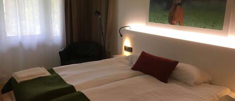 Quarto de hotel com duas camas, uma escrivaninha, uma cadeira, um abajur e um quadro na parede.