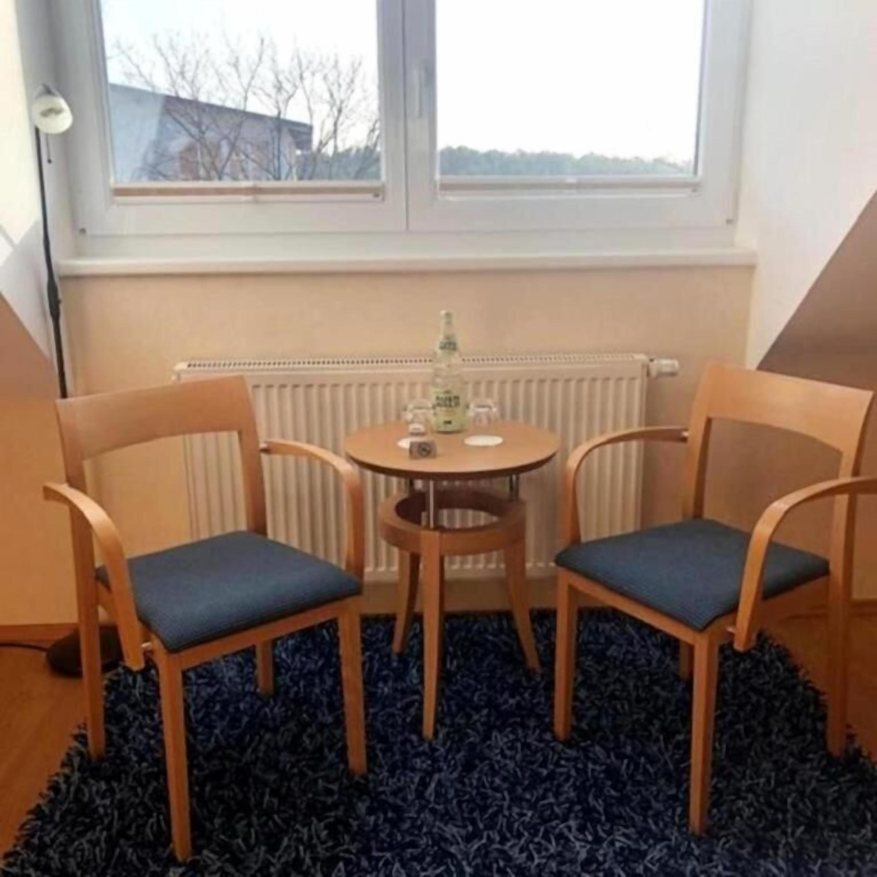 Quarto com duas cadeiras de madeira com almofadas azuis, uma mesa redonda pequena e um radiador.