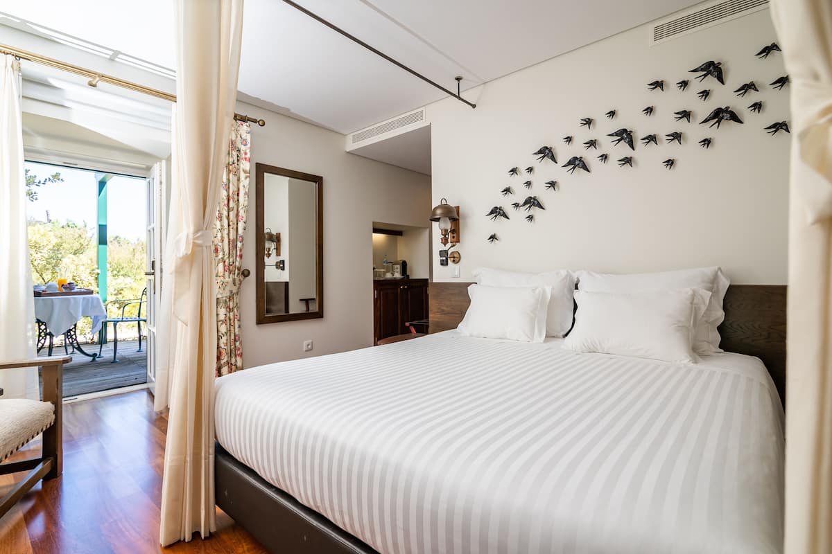 Quarto com uma cama grande, cabeceira de madeira, decoração de pássaro na parede e vista para o exterior.