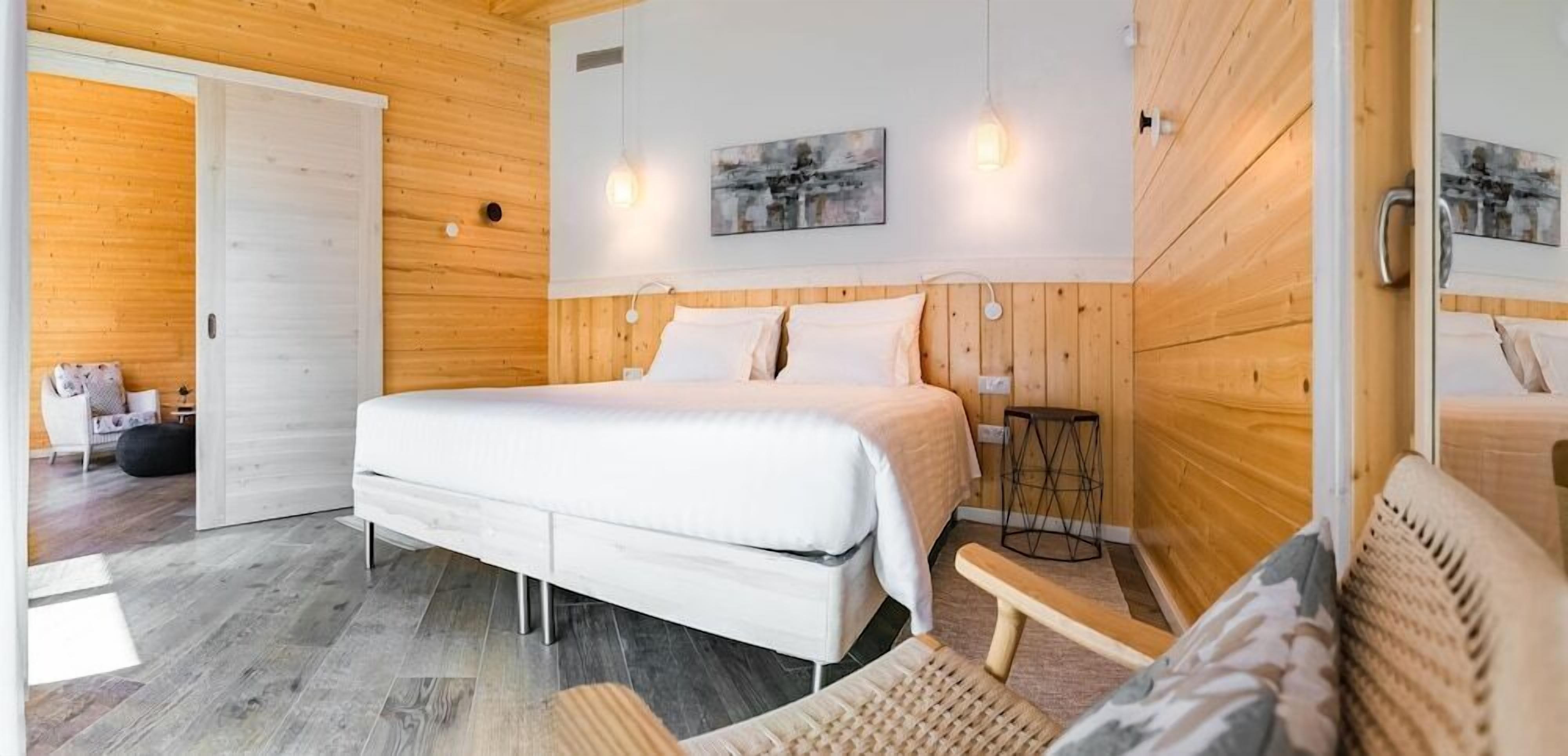 Quarto moderno com cama grande, paredes de madeira e uma pequena mesa de cabeceira.