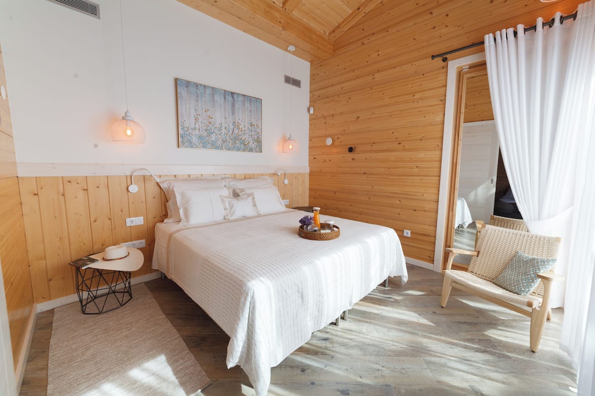 Quarto com painéis de madeira, cama, mesa de cabeceira e uma cadeira.