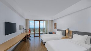 Quarto de hotel com duas camas, uma escrivaninha, televisão e varanda com vista.
