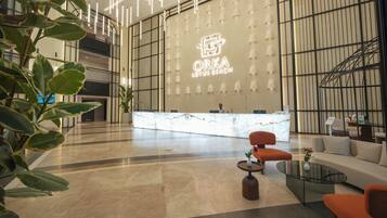 Uma área de recepção moderna com balcão de mármore, um recepcionista e uma área de estar com cadeiras laranja e uma mesa de centro de vidro.