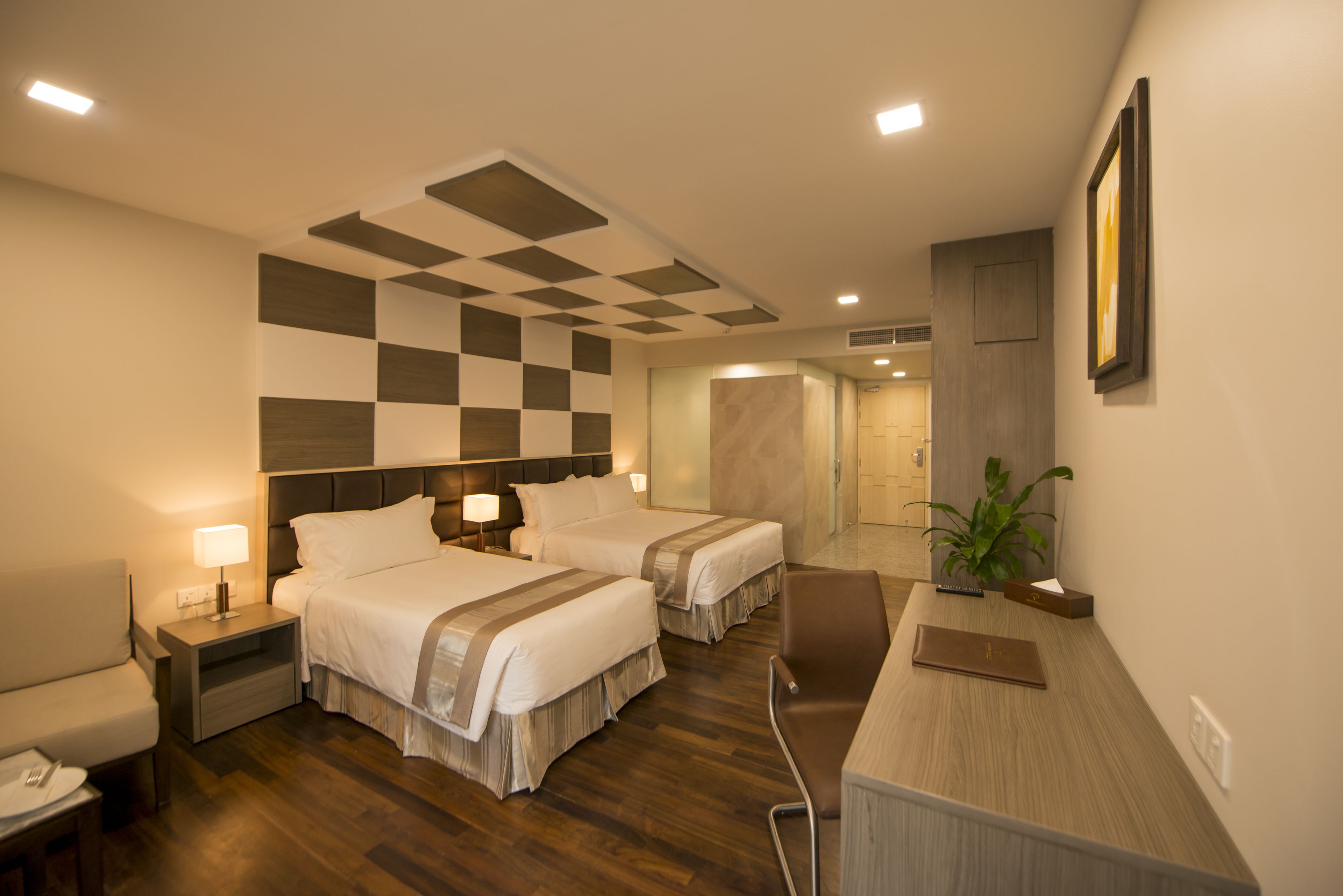 Quarto de hotel com duas camas, uma escrivaninha e uma mesa de cabeceira.