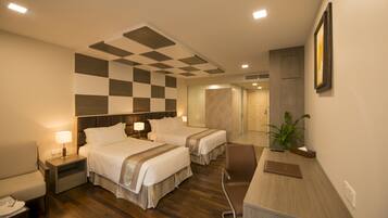 Quarto de hotel com duas camas, uma escrivaninha e uma mesa de cabeceira.