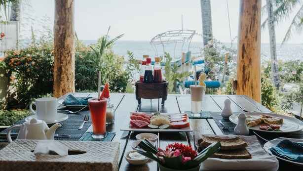Mesa posta para o café da manhã com vista para o oceano, incluindo pratos de comida, bebidas e temperos.