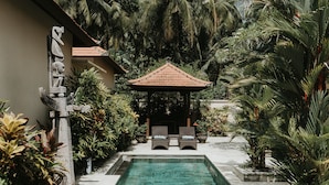 Área de piscina com espreguiçadeiras, um gazebo e uma escultura de pedra.