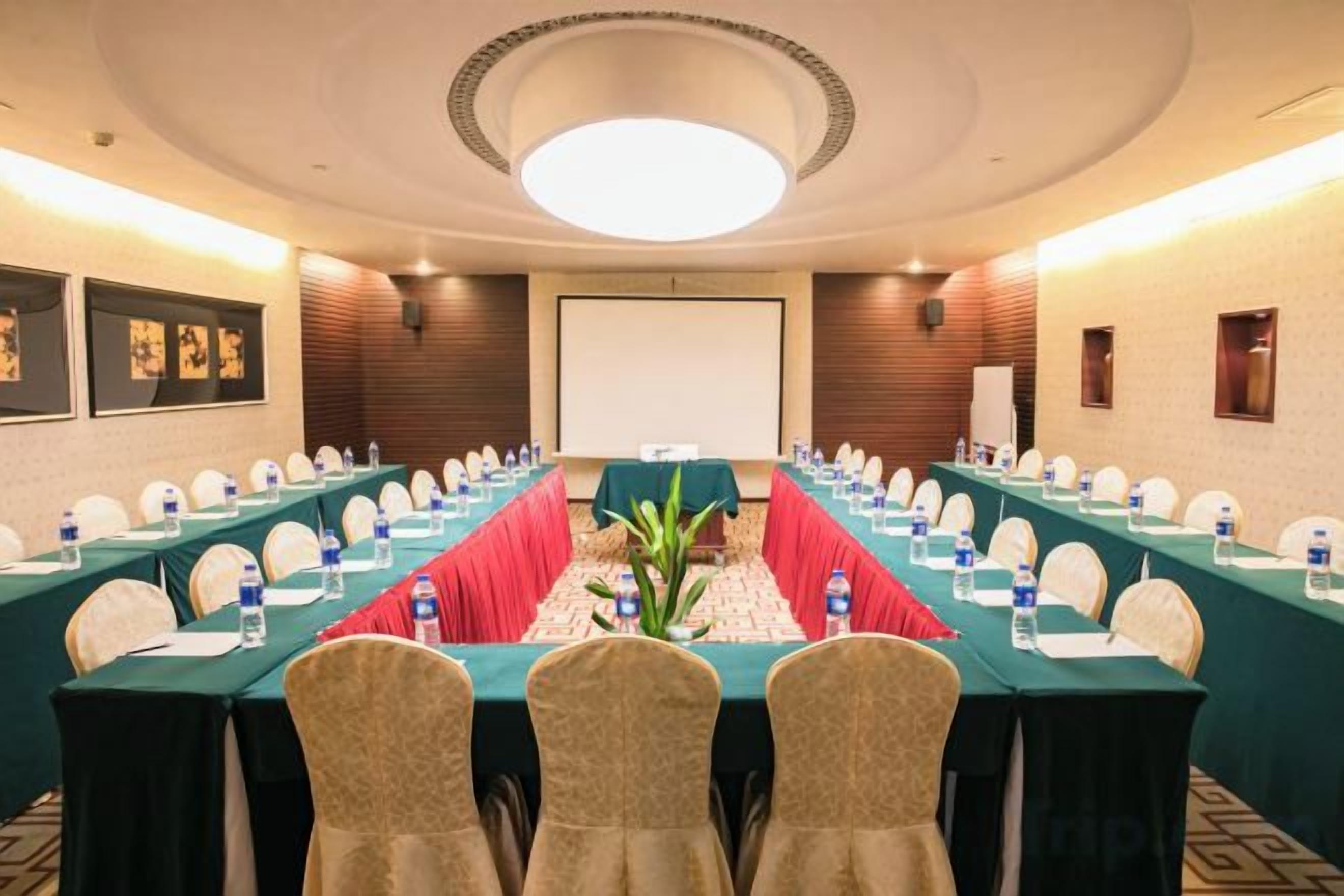 Uma sala de conferência com uma mesa comprida, cadeiras, garrafas de água e uma tela de projetor.