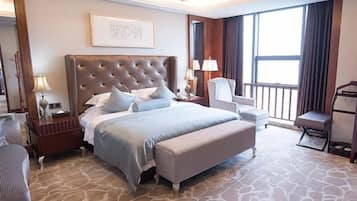 Quarto de hotel com uma cama grande, área de estar, escrivaninha e vista para o exterior.