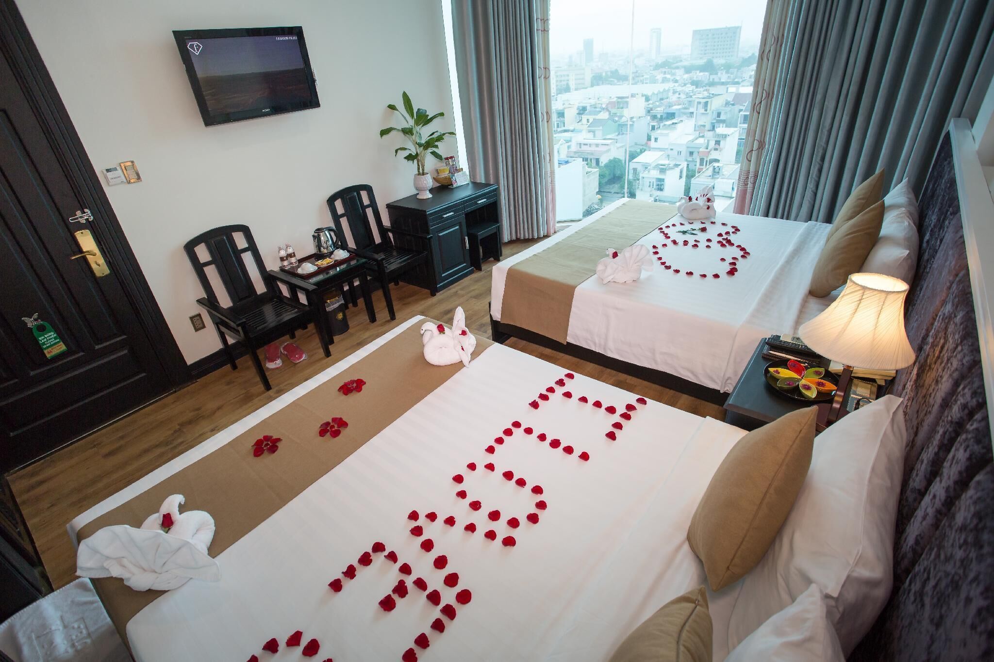 Quarto de hotel com duas camas, uma escrivaninha, uma cadeira, uma TV e vista para a cidade.