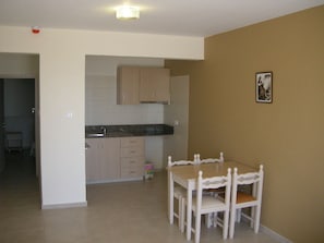 Uma cozinha com armários claros, bancada preta e uma mesa de jantar com cadeiras.