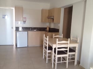 Uma cozinha compacta com geladeira, pia e armários de madeira. Há uma mesa de jantar com quatro cadeiras.