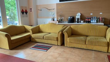 Um saguão de hotel com sofás listrados de amarelo, um espaço para café e uma grande janela com vista para árvores e um castelo.