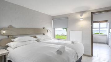 Quarto com cama, mesa de cabeceira, janela com vista para o mar e porta que dá para área externa.